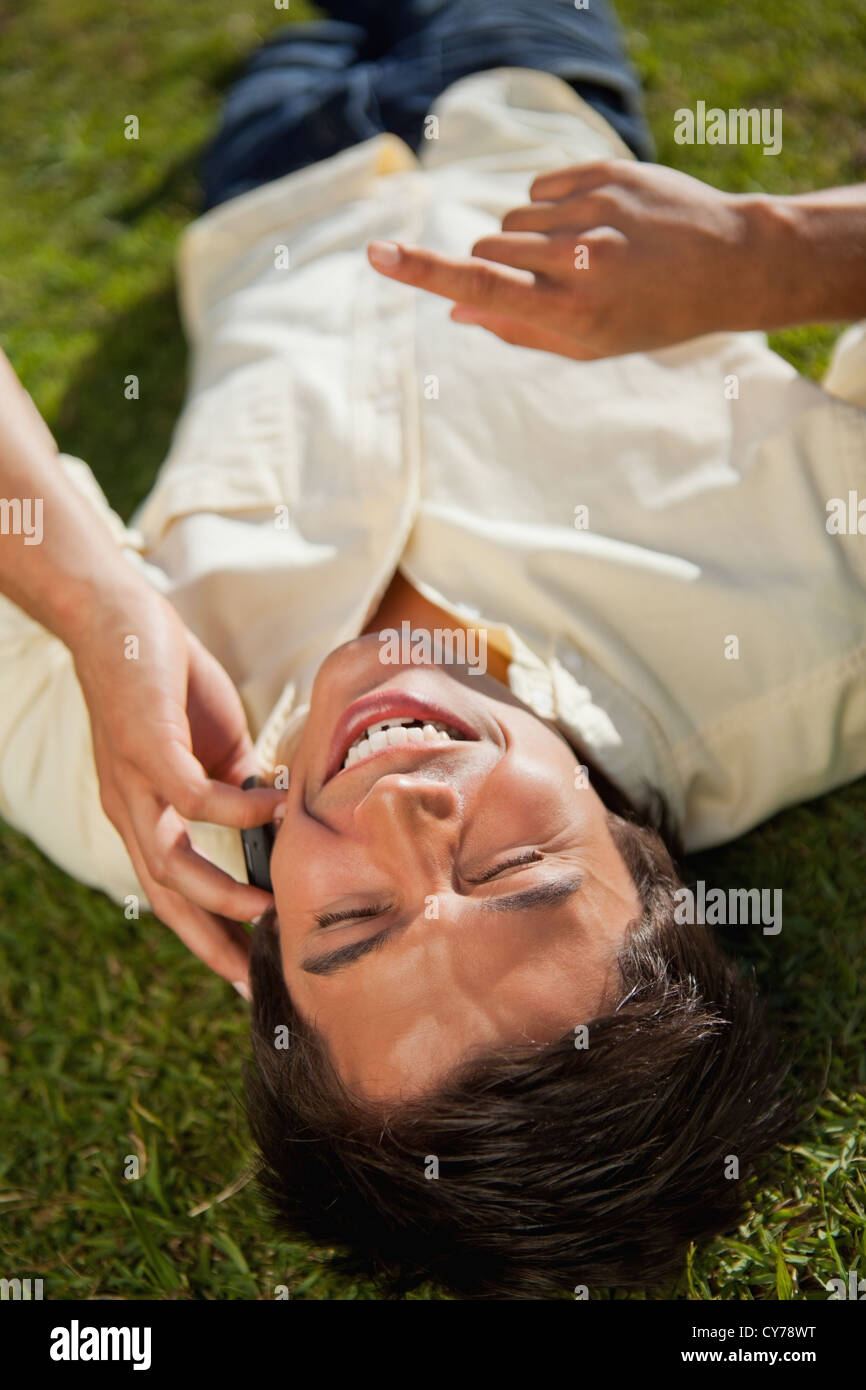 Man with his hand raised laughing while using a phone as he lies down ...