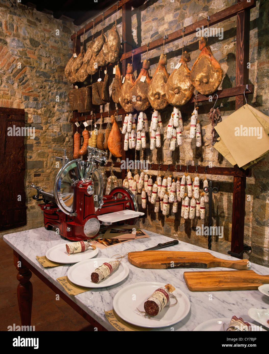 Salami tasting, with hams, salami and other cured meats hanging up ...