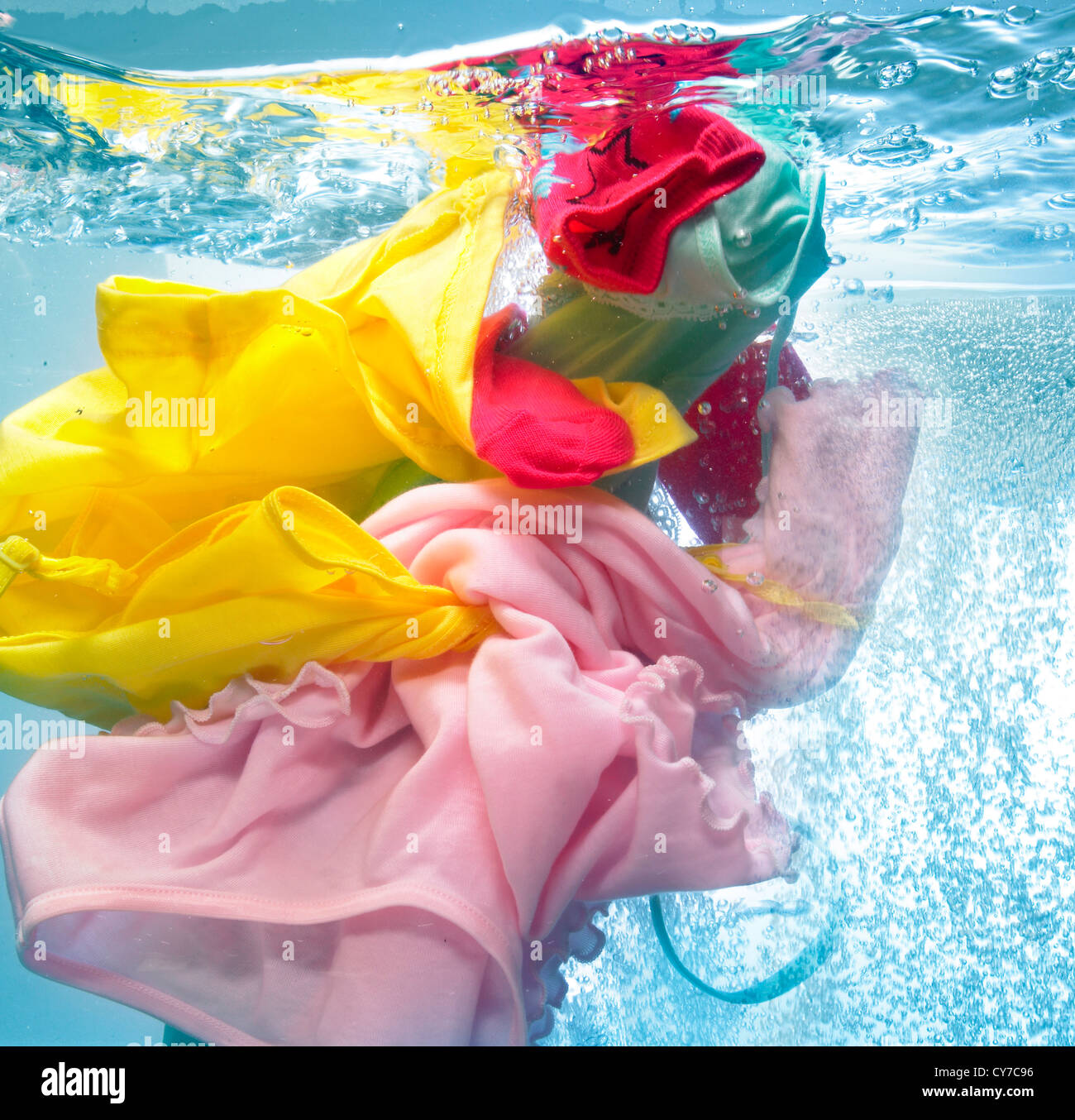 brightly colored clothes being agitated in water with water bubbles and ...
