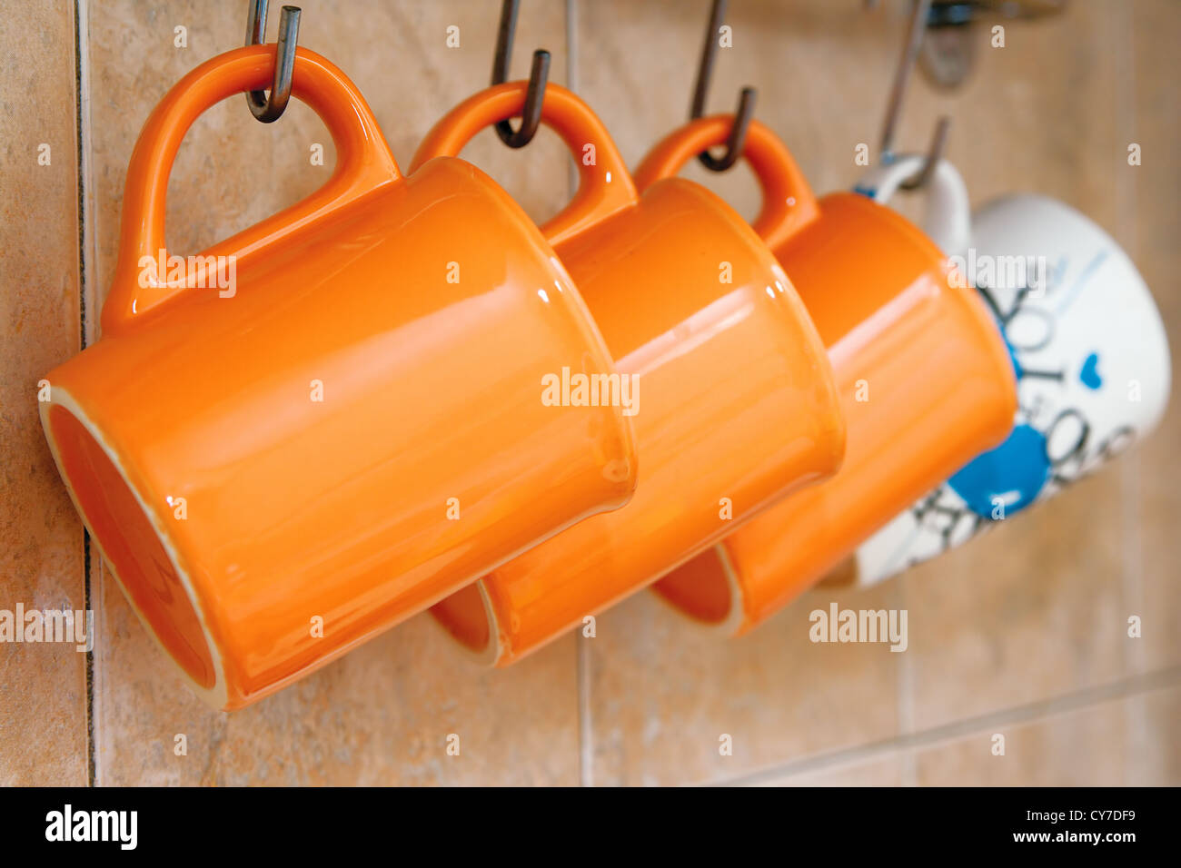 Tea cup orange hang on hooks on the wall Stock Photo - Alamy