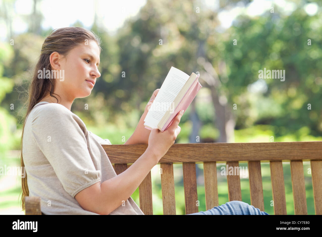 Side view of woman reading while sitting on a park bench Stock Photo ...