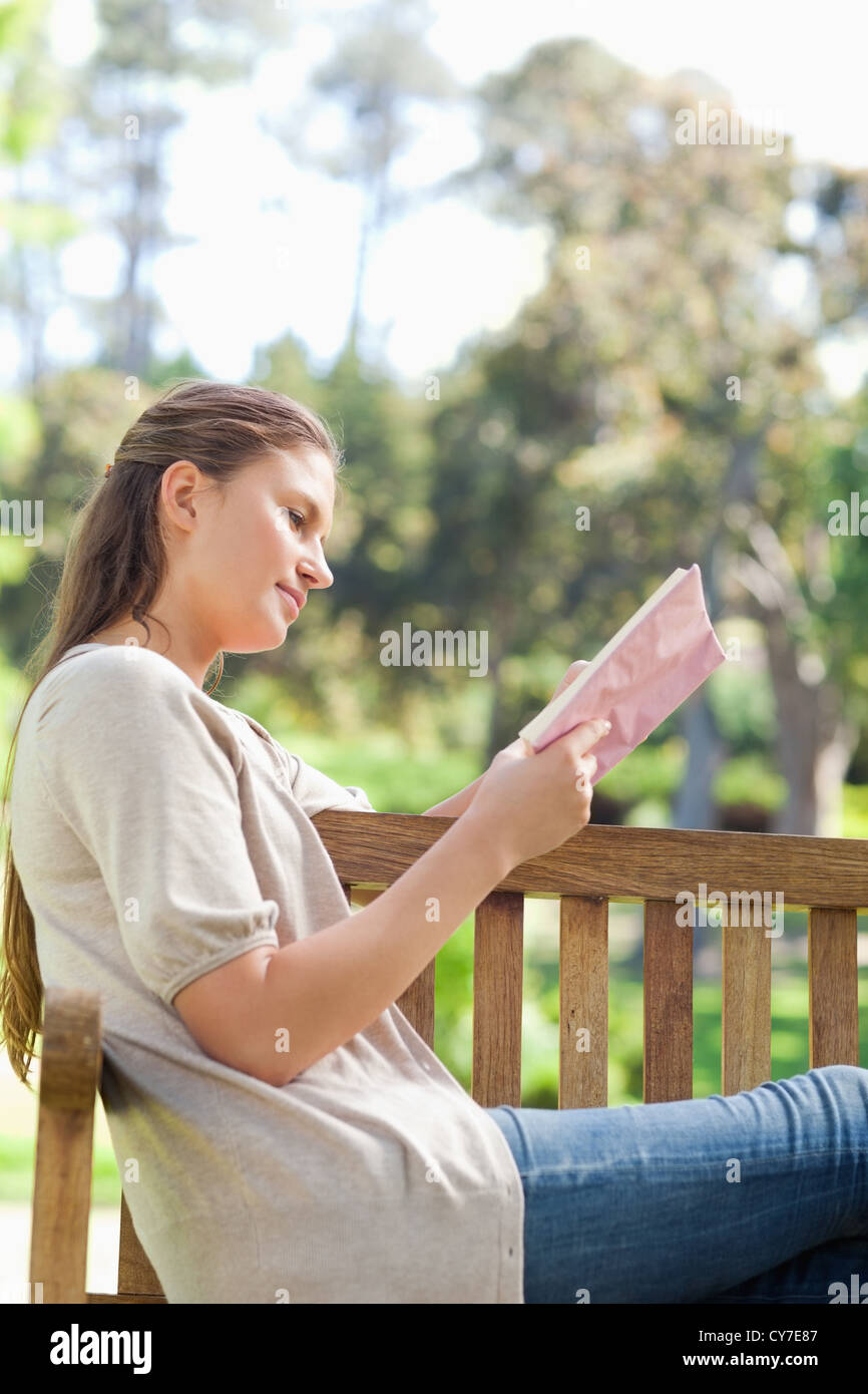 Side view of a woman reading a book on a park bench Stock Photo - Alamy