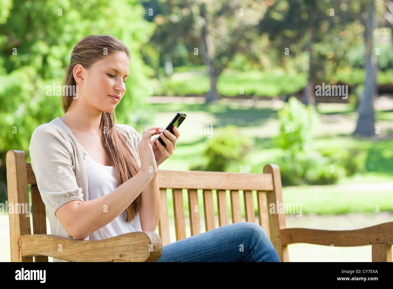 Woman writing a text message on her cellphone while on a park bench ...