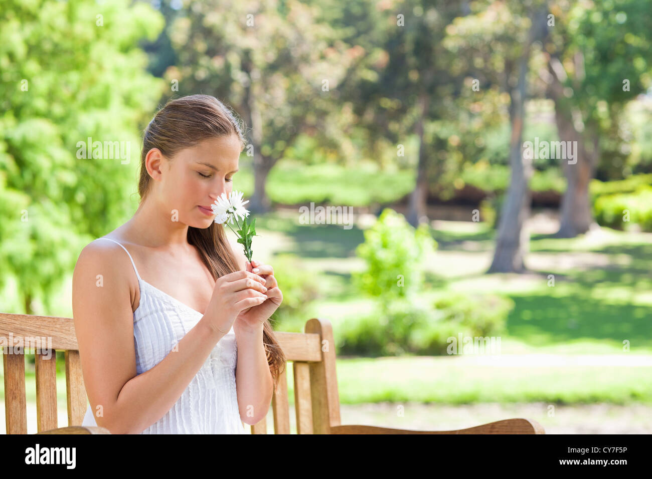 Woman smelling a flower while sitting on a park bench Stock Photo - Alamy