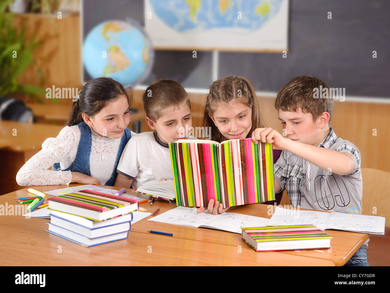 Four elementary aged pupils reading book in classroom Stock Photo - Alamy