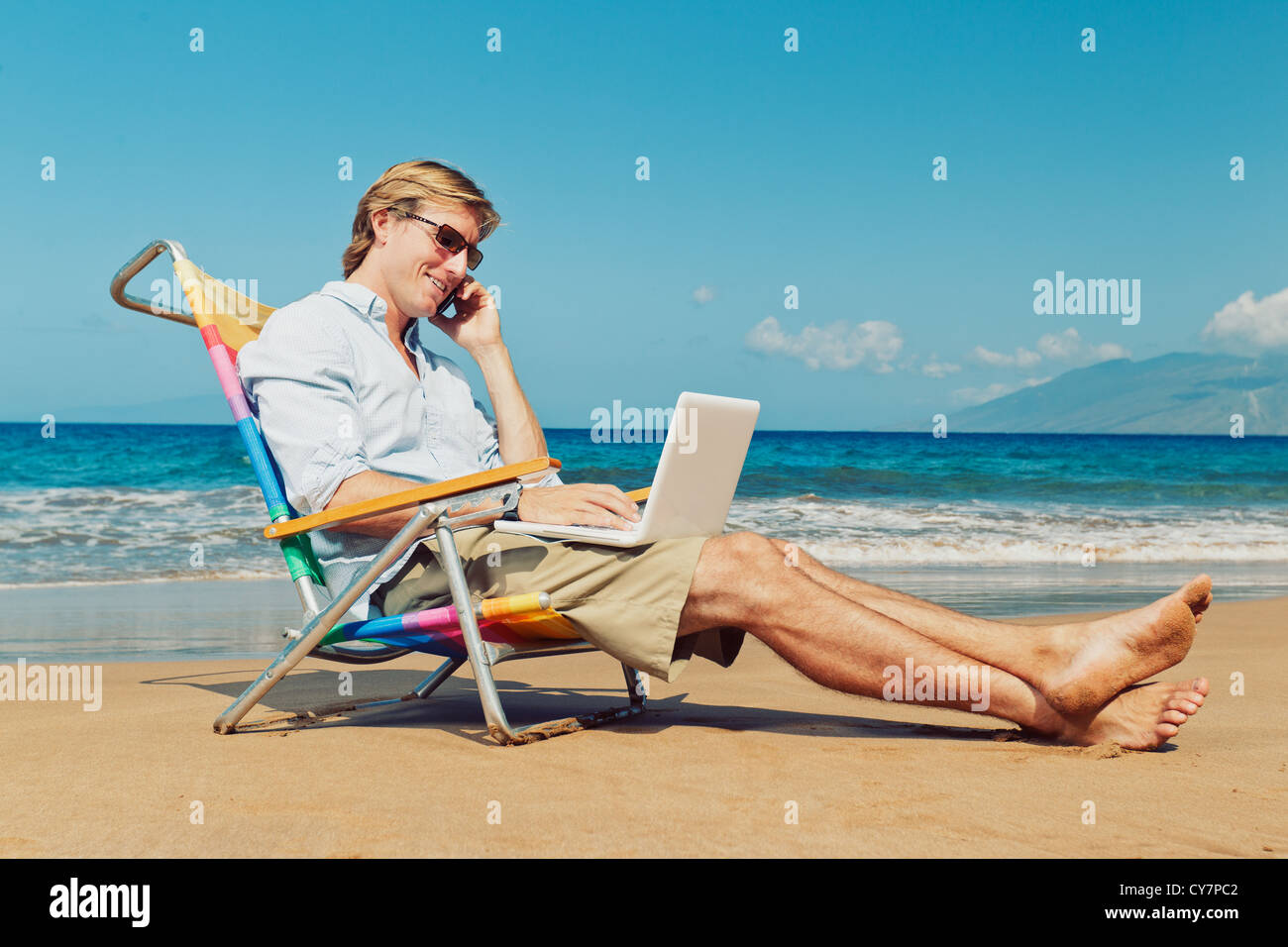 Business man calling by cell phone and working on computer at the beach ...