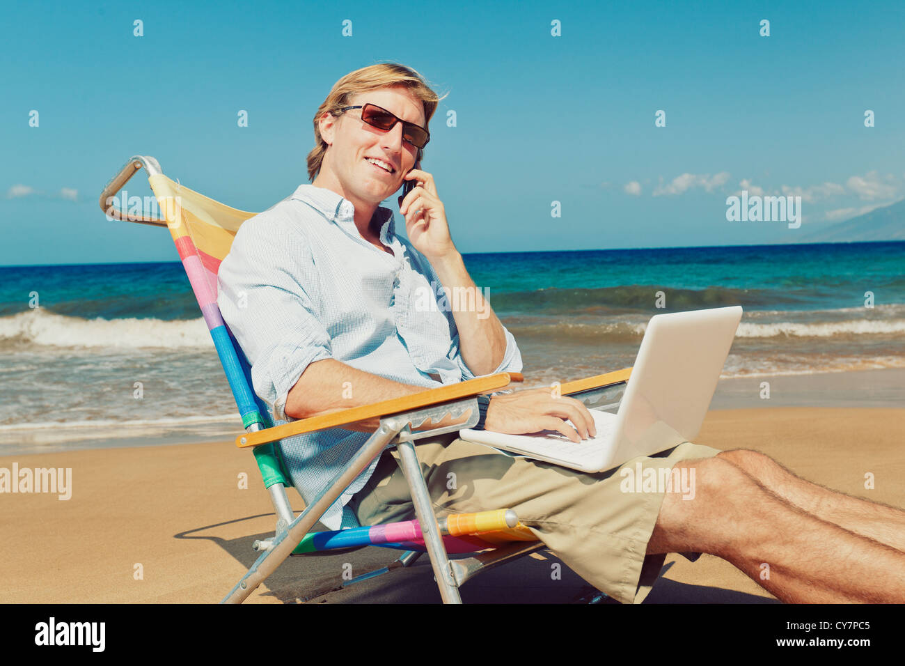 Business man calling by cell phone and working on computer at the beach ...