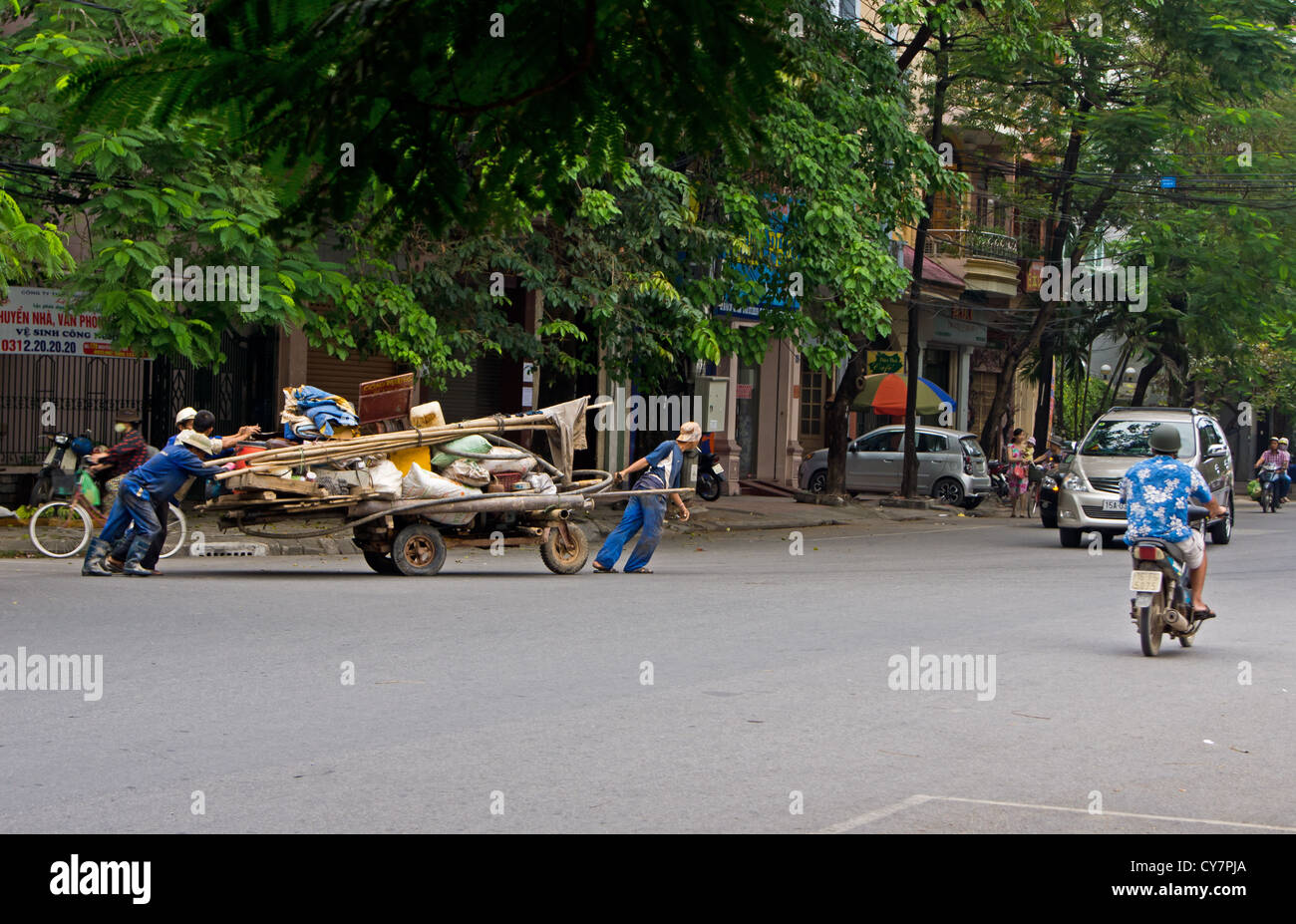 Vietnamese workers push the work cart across a busy road in Hai Phong ...