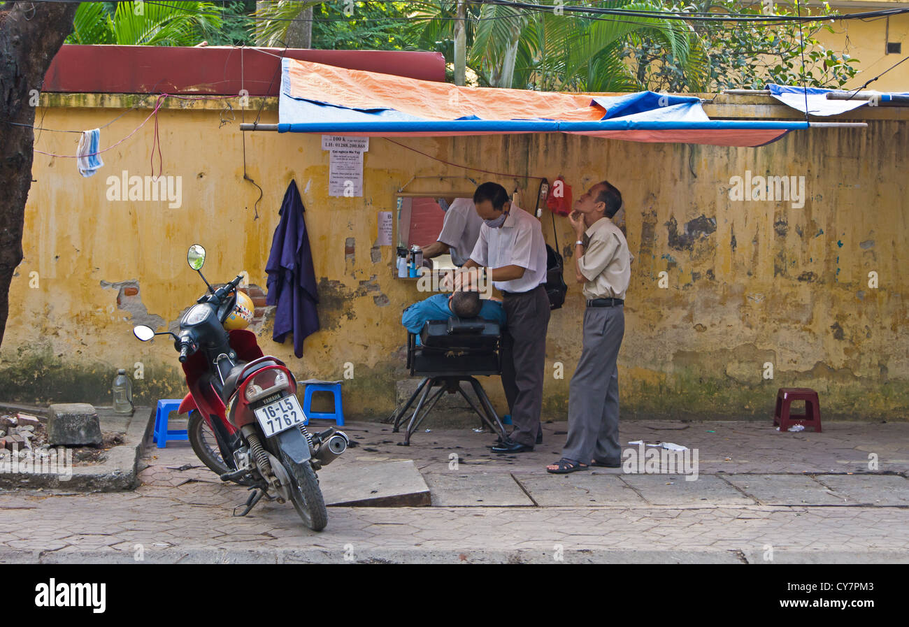 A man getting a hair cut and shave on the road side from a street ...