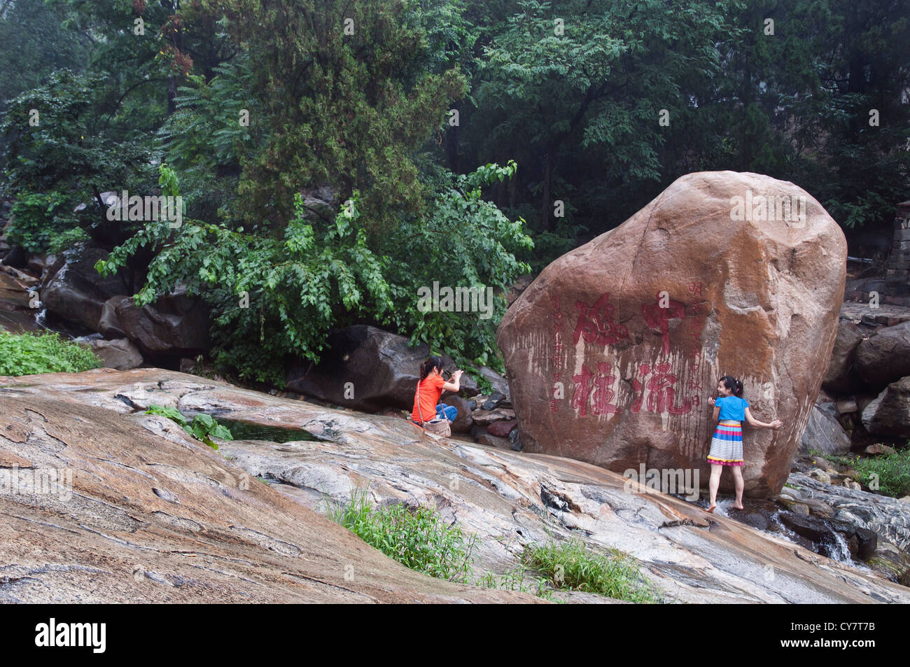 Two girls pose next to a huge boulder and its inscription on Mount Tai ...