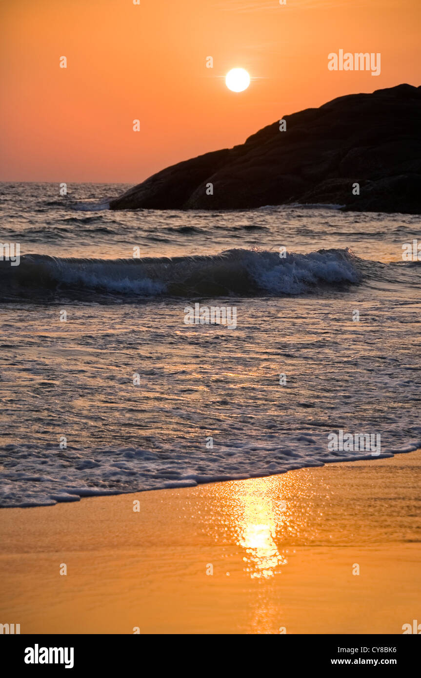 Vertical view of the sun setting over the crashing waves in Kerala ...