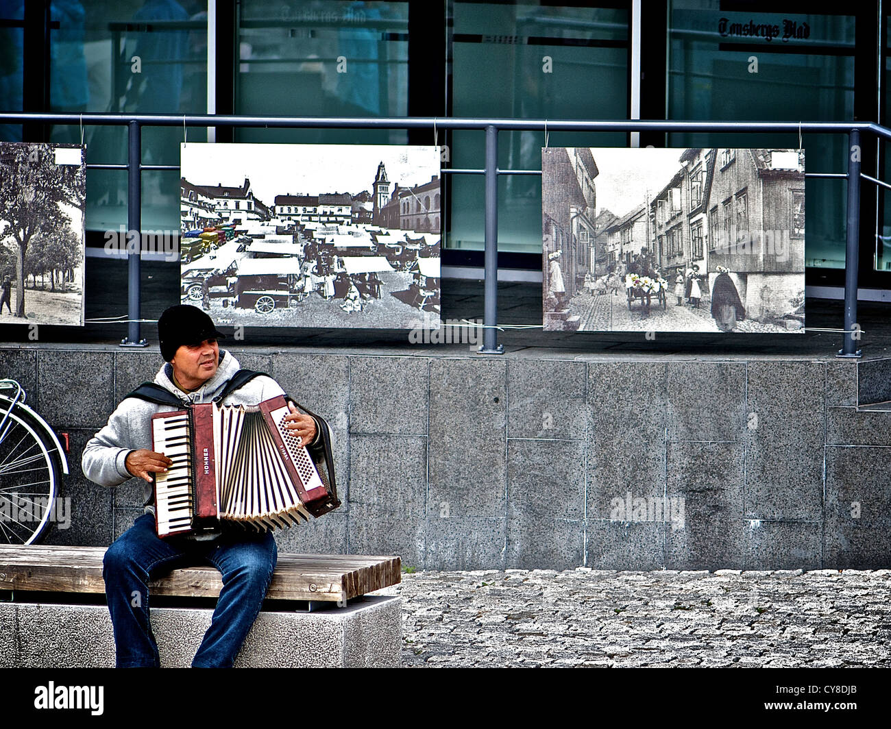 An accordion busker plays in a stone street with scenic paintings in ...