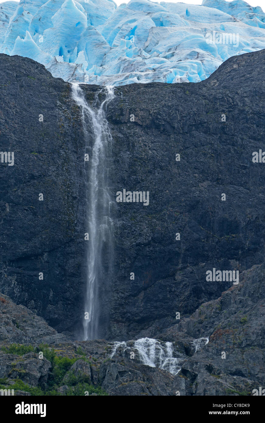 A hanging glacier ice with melt water spilling down the bare rocks ...