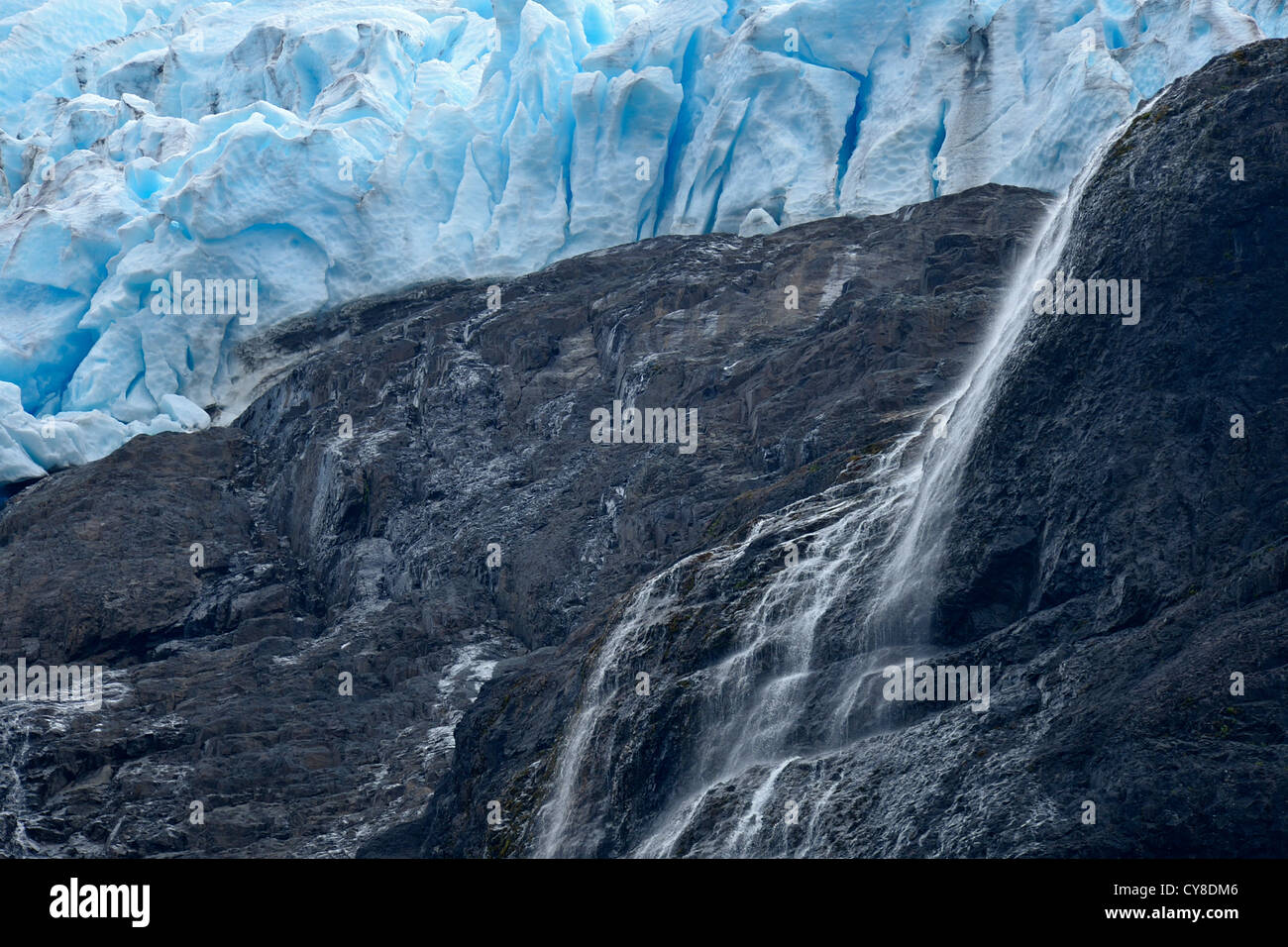 A hanging glacier ice with melt water spilling down the bare rocks ...