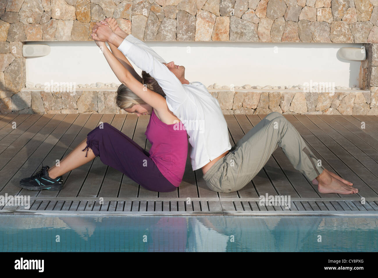 Young couple sitting back to back at poolside stretching Stock Photo ...