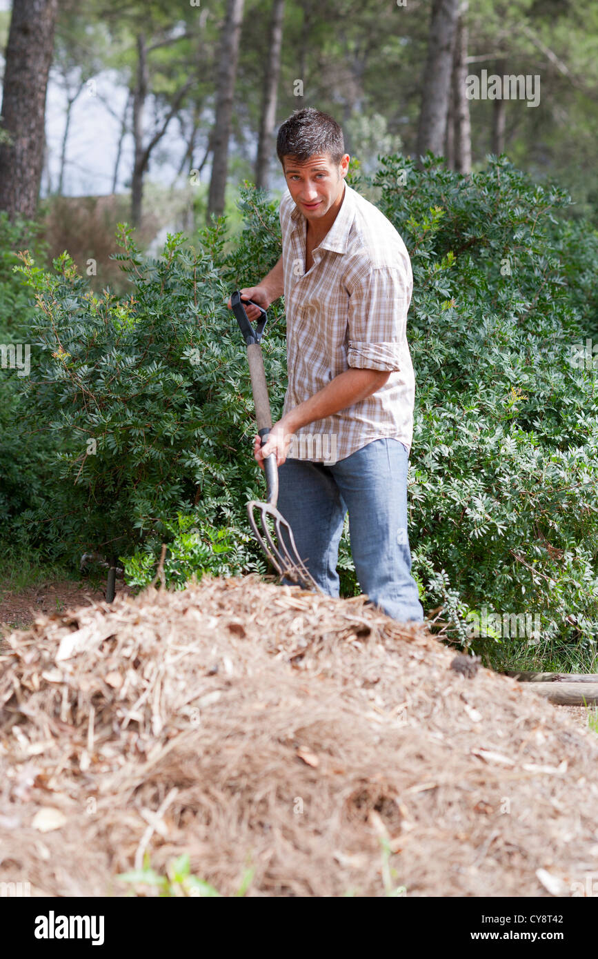 Man standing by heap of straw, holding gardening fork Stock Photo - Alamy