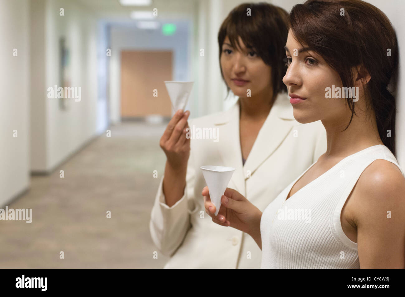 Businesswomen taking break and drink from disposable cups in hallway ...