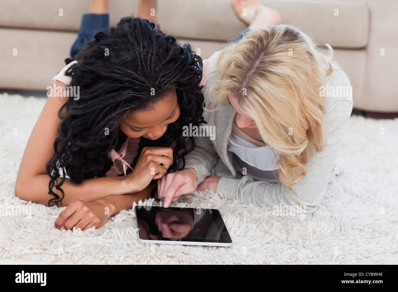 A woman is lying on the floor using a tablet computer while her friend ...