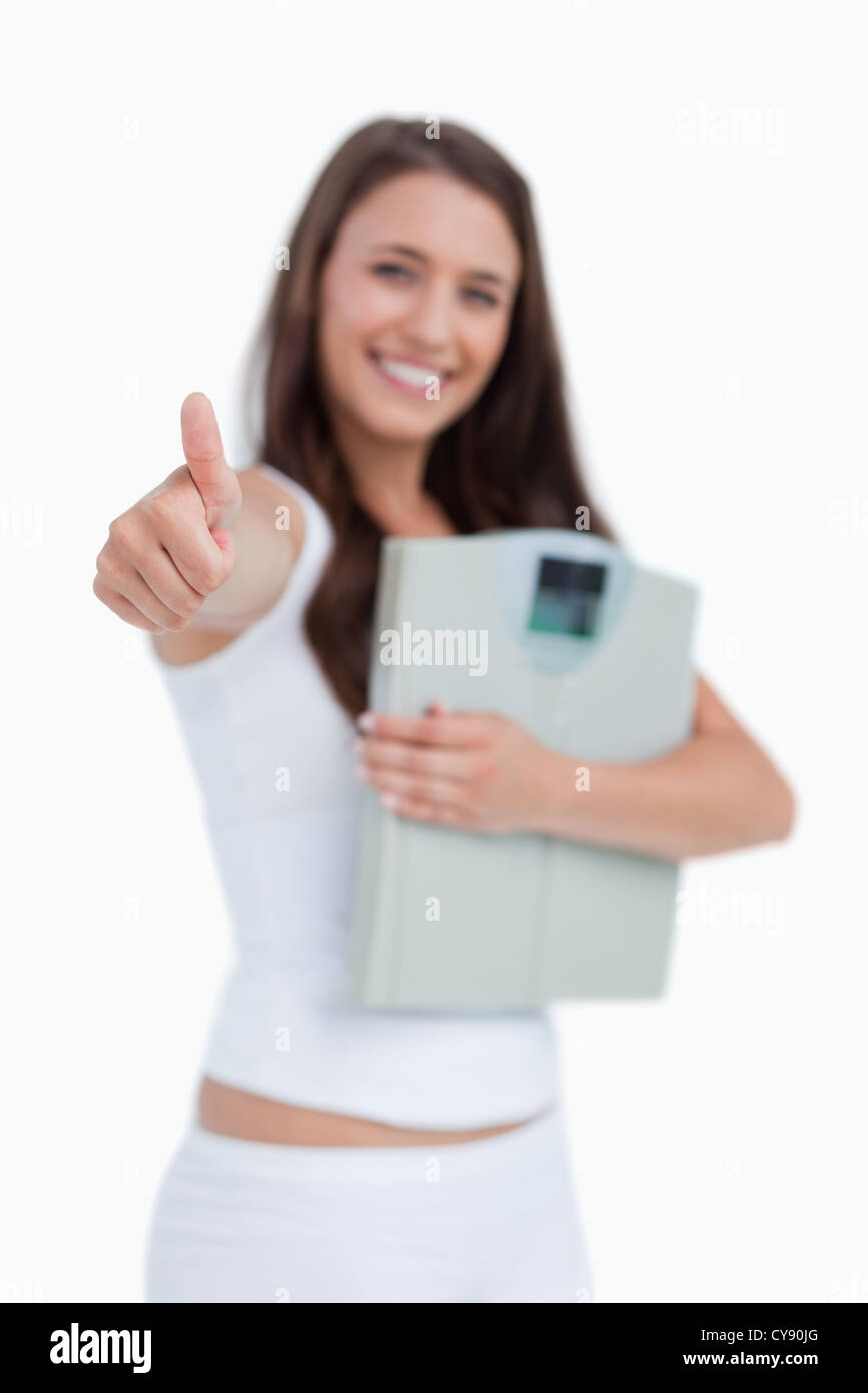 Brunette woman giving the thumbs up while holding a scales Stock Photo ...