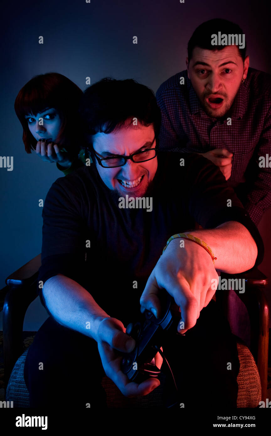 Young emotional man playing video games, two scared persons are hiding ...