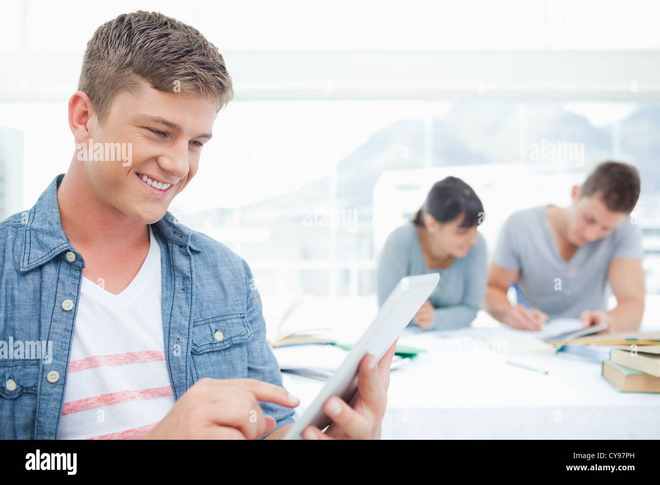 A smiling male using his tablet pc in front of his friends Stock Photo ...