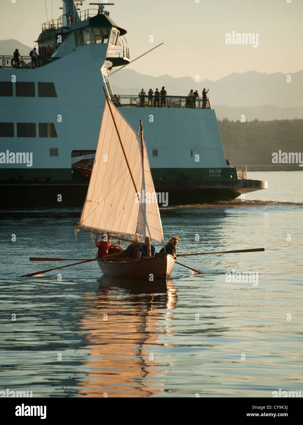 A small sailboat rows past a Washington State Ferry at the coastal town ...