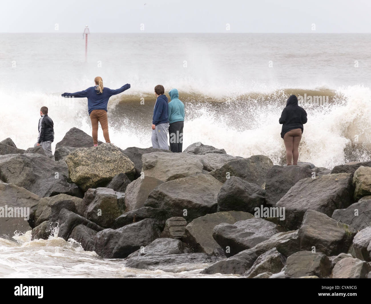 Youg people standing precariously on a rock breakwater wall enjoying ...