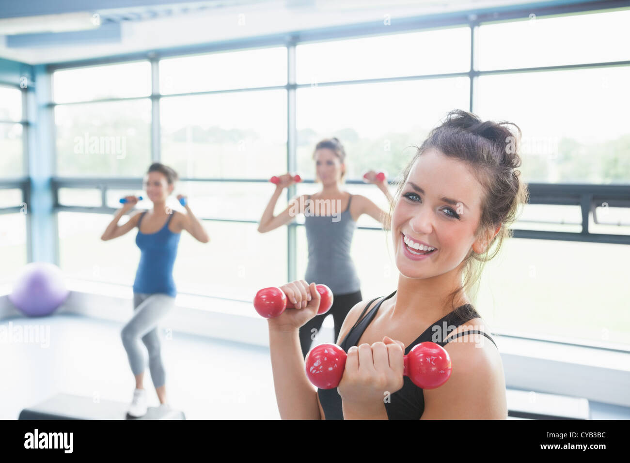 Smiling woman lifting weights while women doing aerobics Stock Photo ...