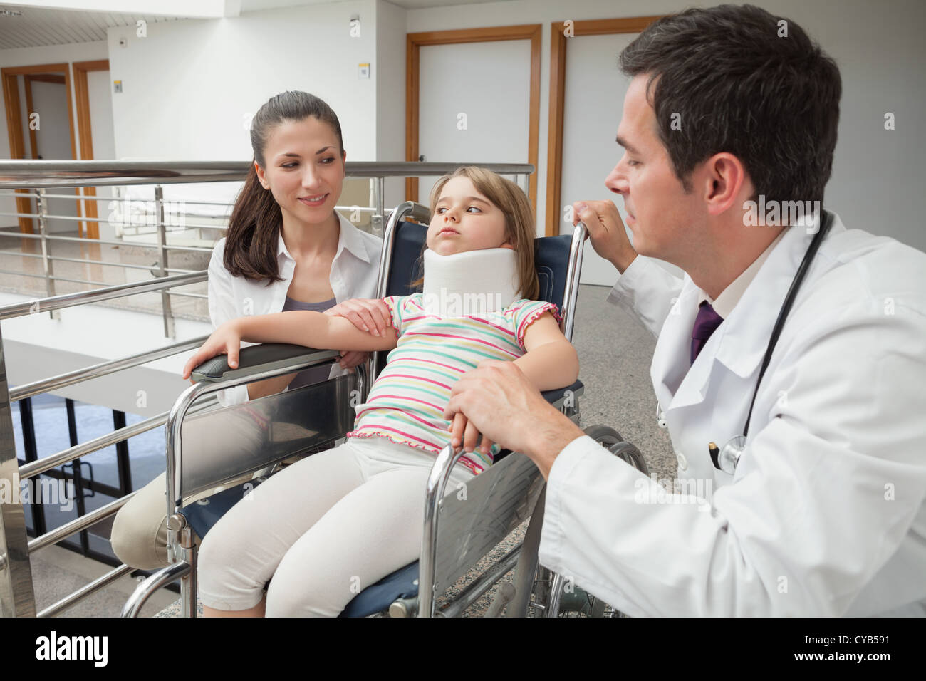 Mother and doctor crouch next to child in wheelchair with neck brace ...