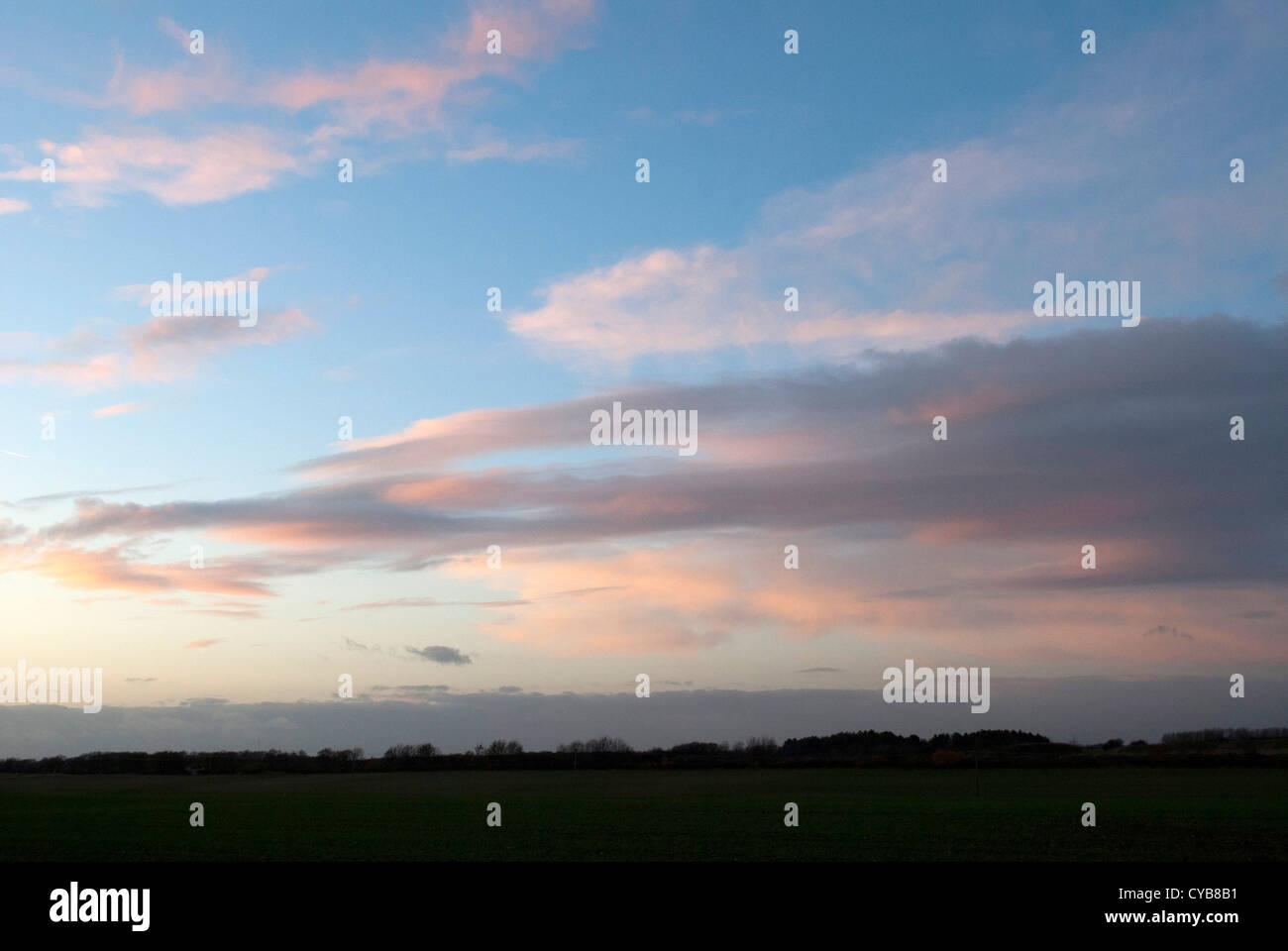Dark fields in shadow beneath pale sky with pink clouds near sunset ...