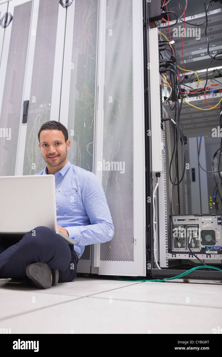 Man sitting on floor using laptop to check servers Stock Photo - Alamy