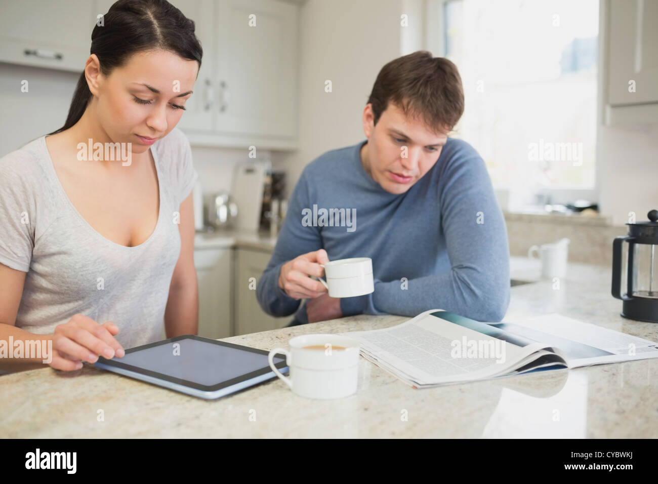 Two people reading from tablet pc and newspaper Stock Photo - Alamy