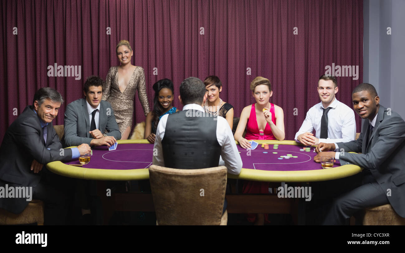 Smiling group sitting around poker table Stock Photo - Alamy