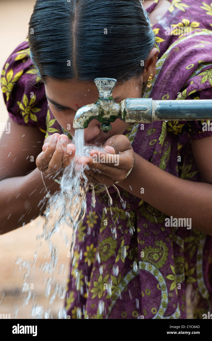 Indian girl drinking from a communal water tap in rural indian village ...