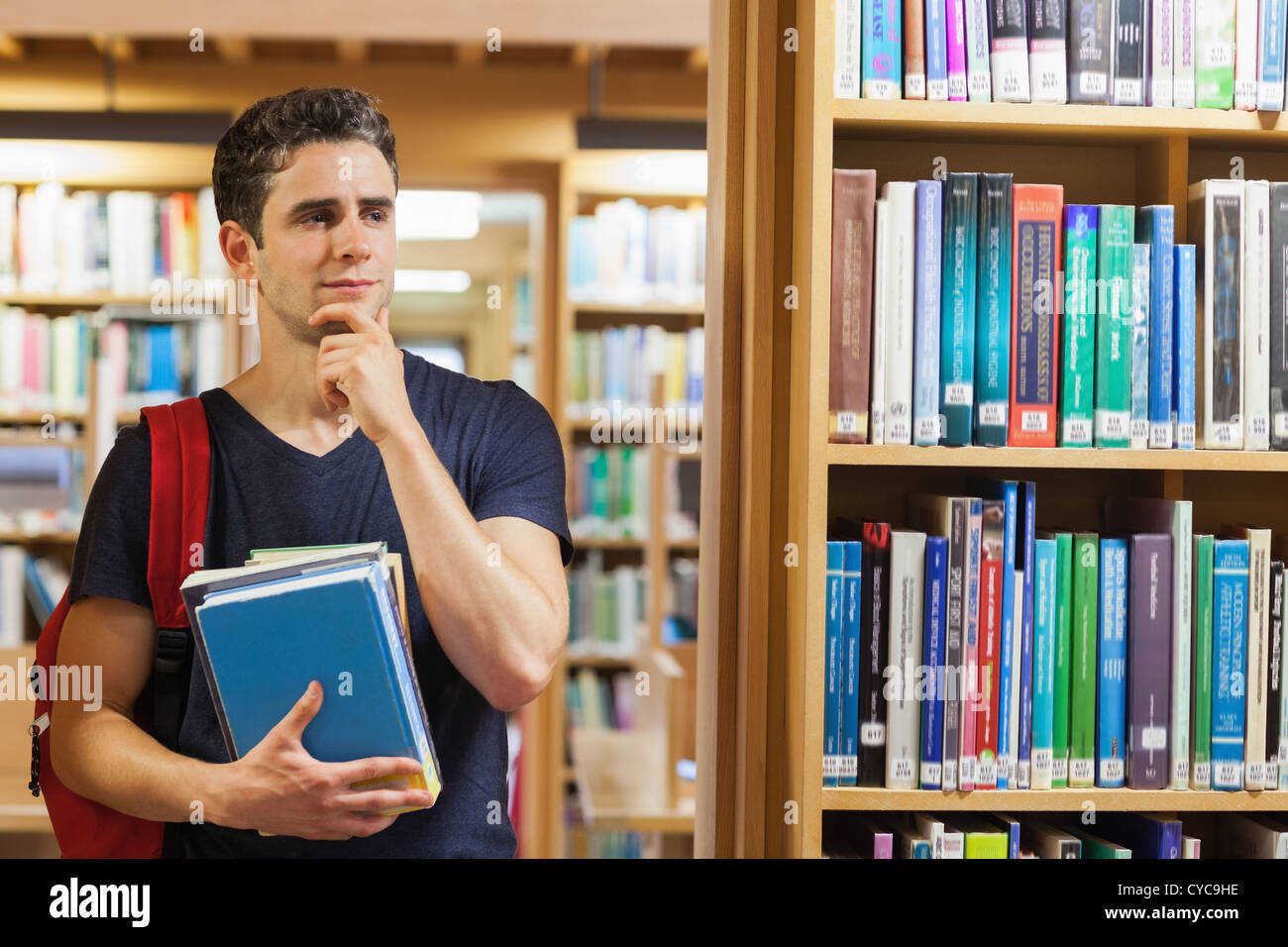 Student standing at the bookshelf thinking Stock Photo - Alamy