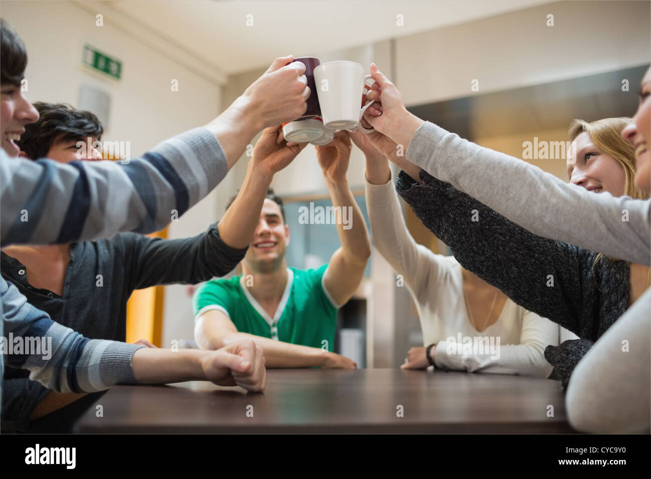 Students sitting around the table clinking mugs Stock Photo - Alamy