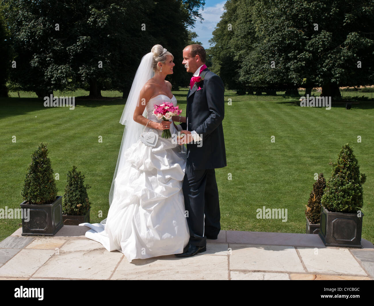 A bride and groom tenderly hold hands and look at one another lovingly ...