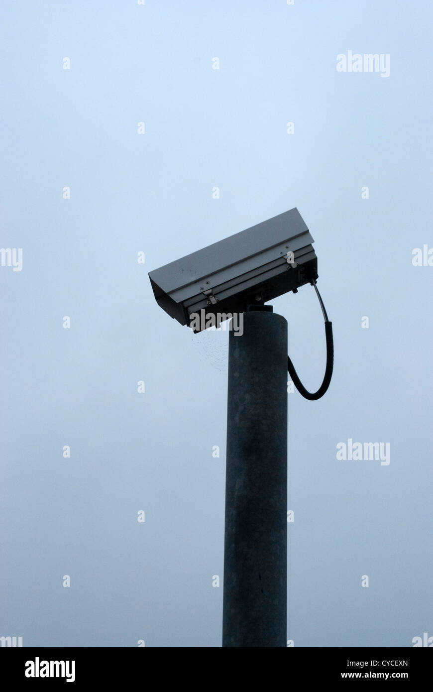 Closed-circuit television (CCTV) camera on a pole silhouetted against a ...