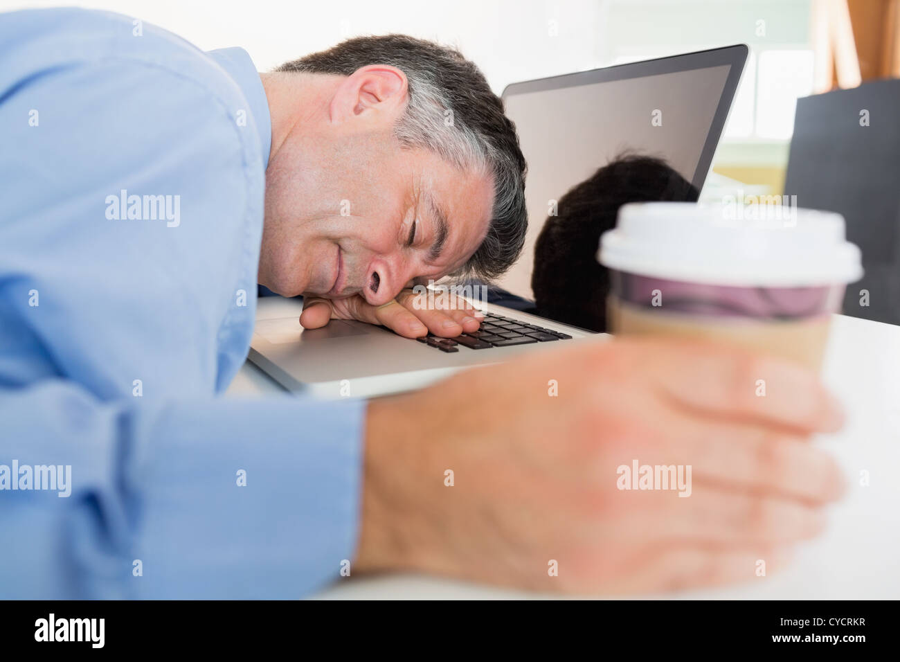 Man sleeping on his laptop while holding coffee Stock Photo - Alamy