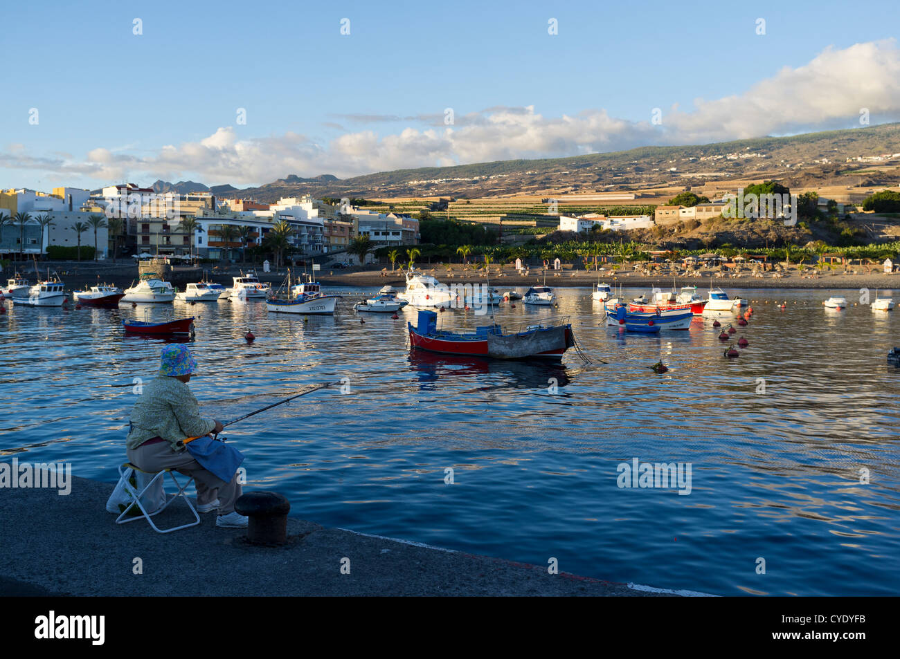 Old lady fishing off the quayside at Playa San Juan harbour, Tenerife ...