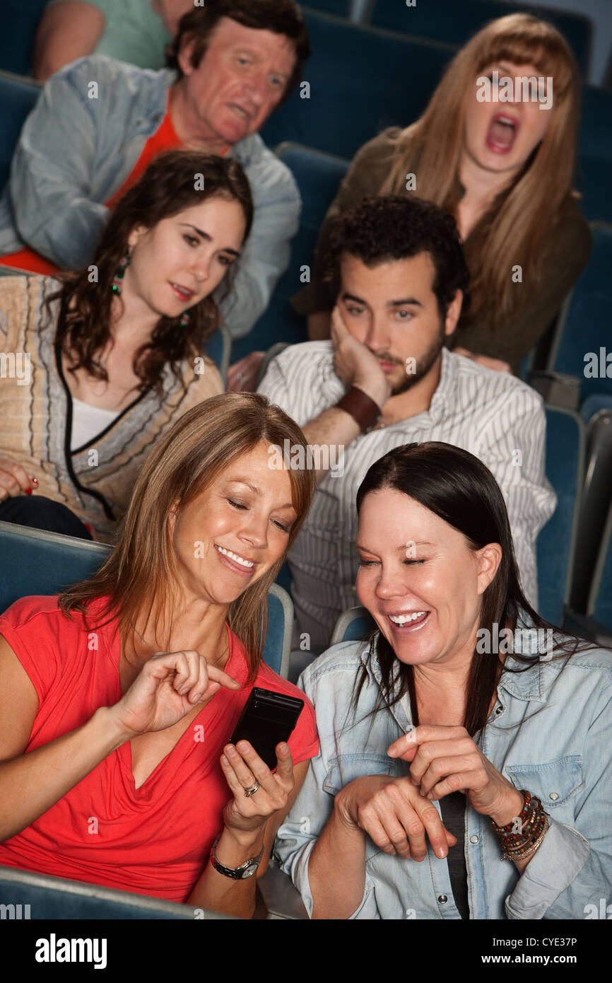 Two women talking in theater with bothered audience Stock Photo - Alamy