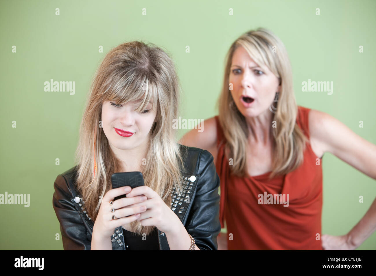 Shocked mom watches teen use phone over green background Stock Photo ...