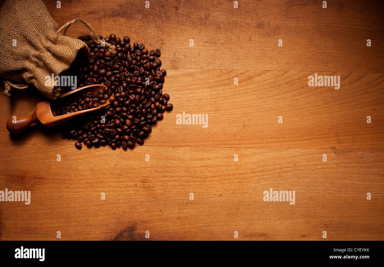 Freshly roasted coffee beans spilling out hessian bag over a wooden scoop and onto a textured ...