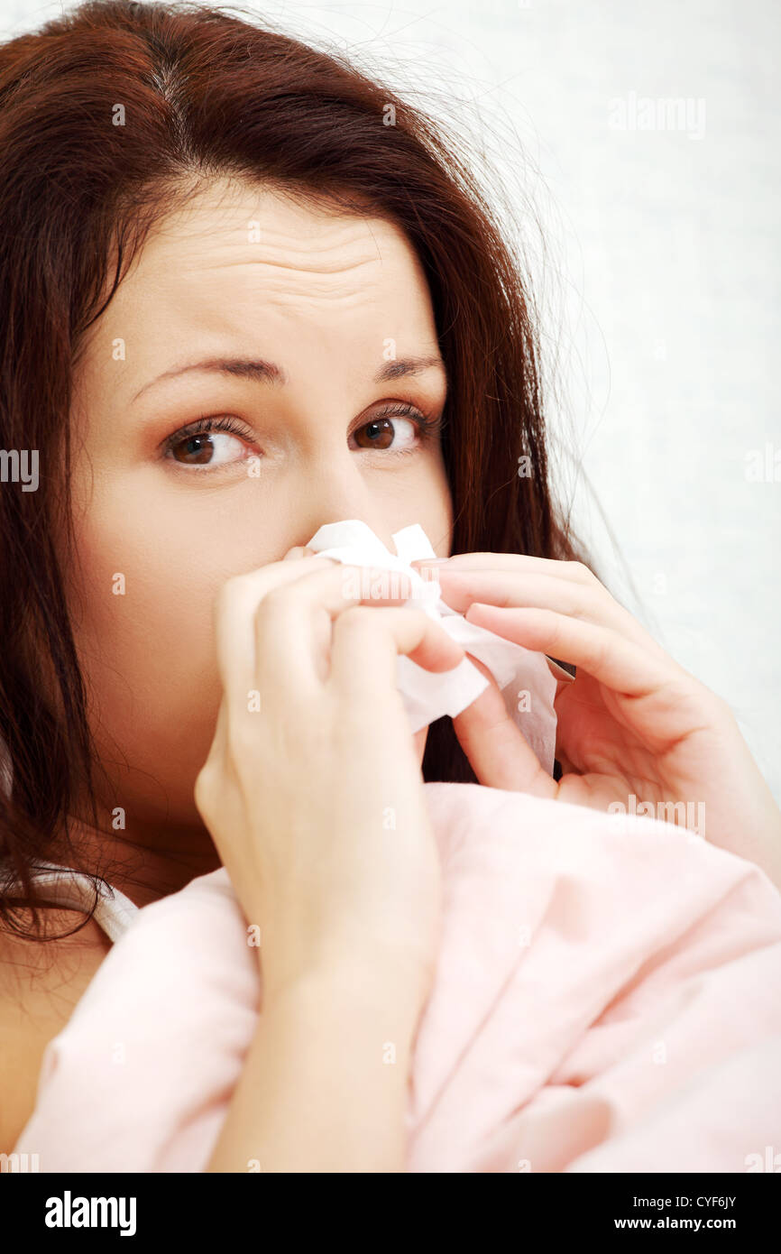 Face closeup of a beautiful young woman lying in bed, having a cold and ...