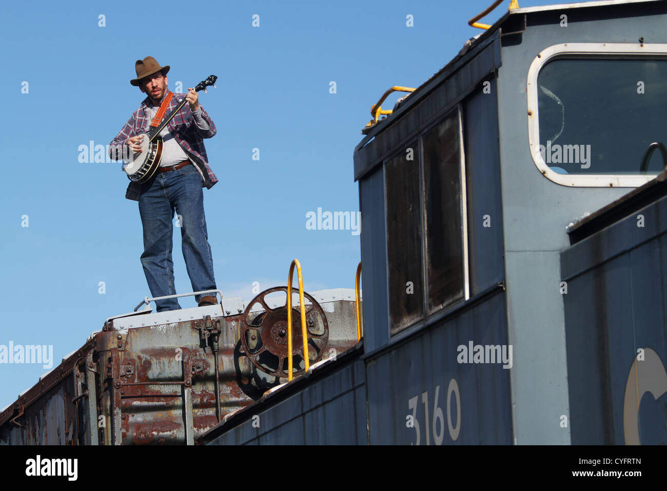 Male model as a hobo playing banjo while standing on a railroad box car ...