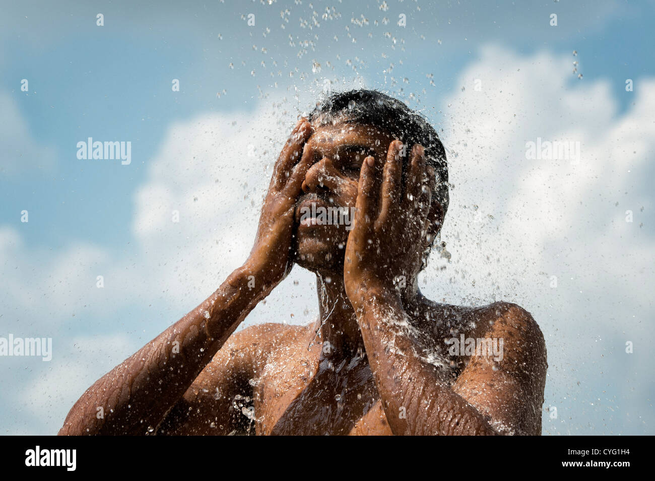 Indian man splashing water on his face against blue sky background ...