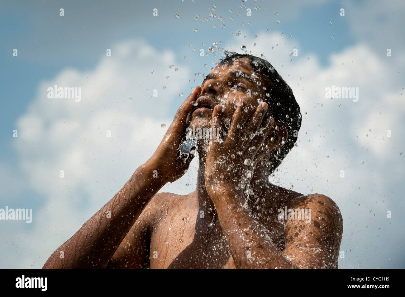 Indian man splashing water on his face against blue sky background ...