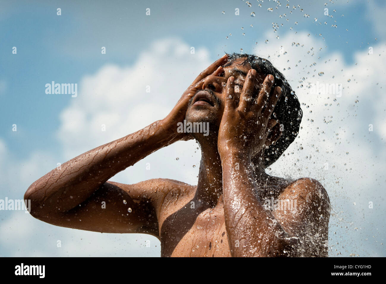 Indian man splashing water on his face against blue sky background ...
