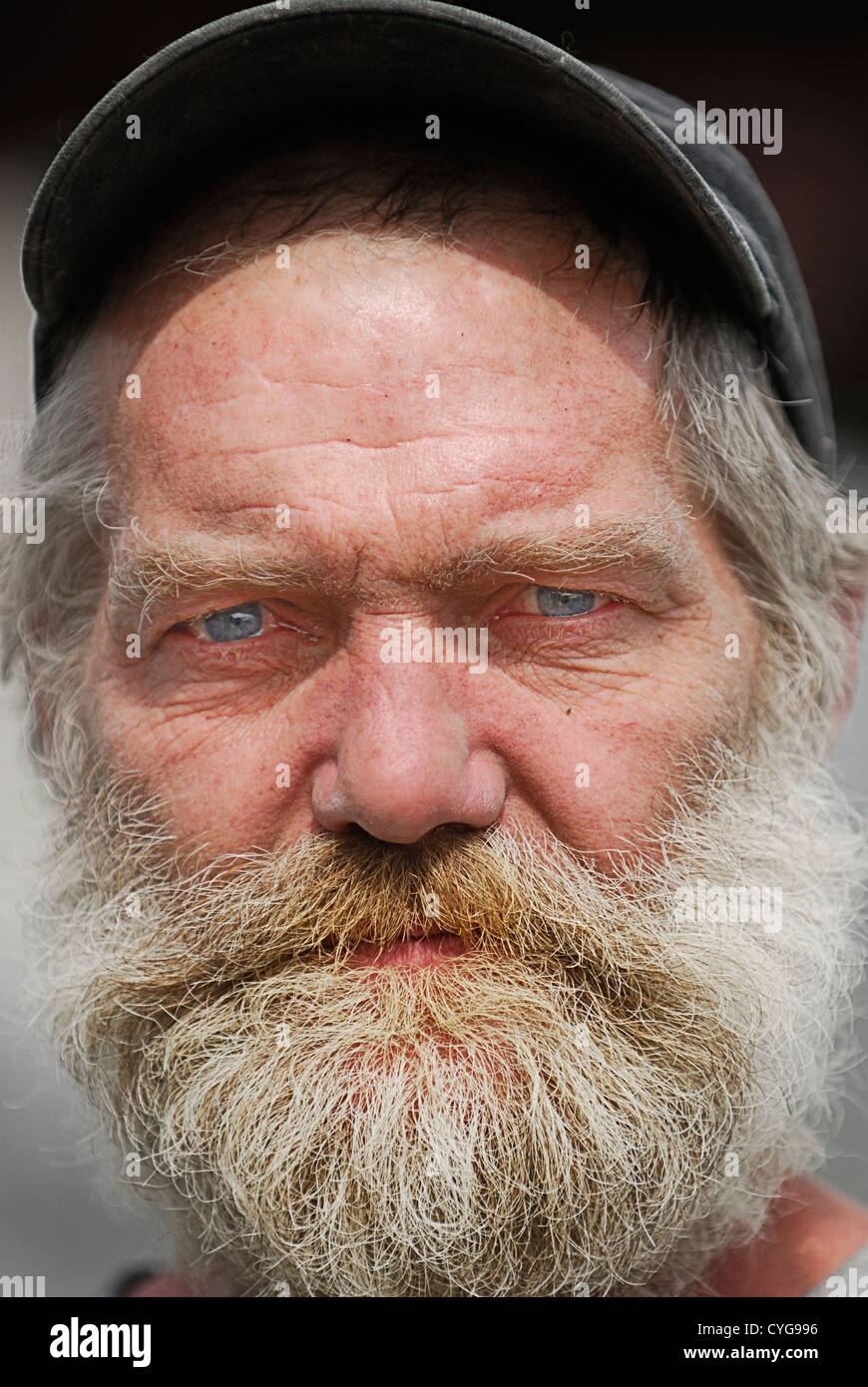 Portrait of an old man not smiling with a gray beard wearing a cap ...