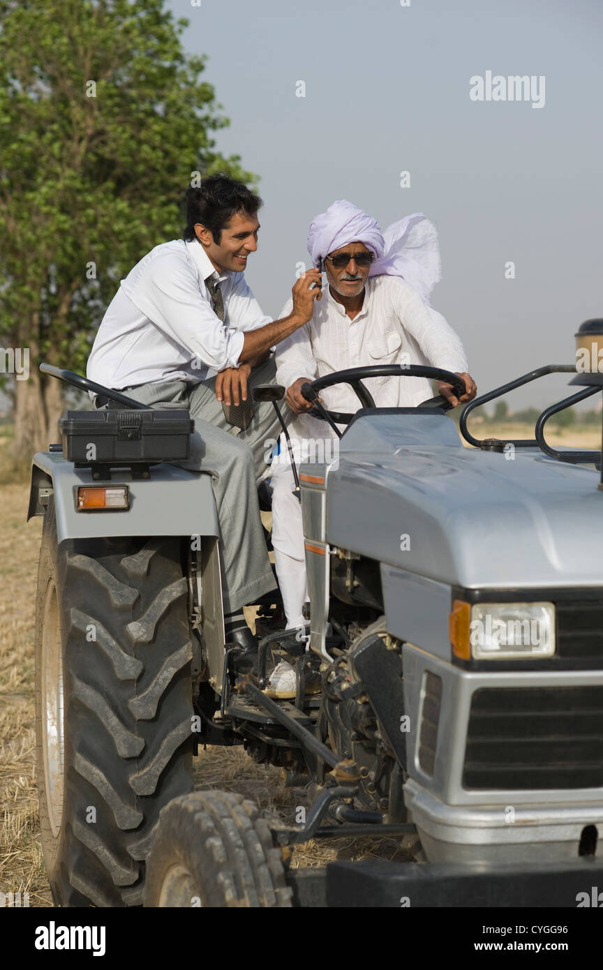 Farmer talking on a mobile phone while driving a tractor with his son ...